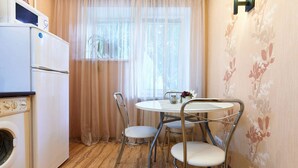 Uma cozinha compacta com máquina de lavar, geladeira, mesa de jantar com quatro cadeiras e janela com cortinas leves.