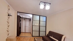 Sala de estar com um sofá marrom, uma pequena mesa de centro de madeira e uma porta de vidro deslizante que dá para um banheiro.