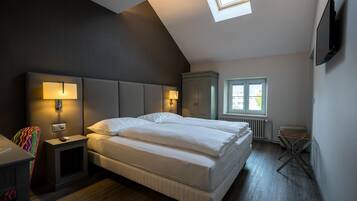 Quarto moderno com claraboia, cama, abajures, radiador e televisão na parede.