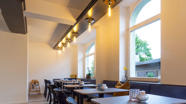Uma sala de jantar moderna com mesas de madeira e cadeiras pretas, janelas amplas e um lustre no teto.
