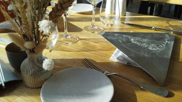 Uma mesa de jantar posta com prato, garfo, faca e um vaso decorativo com flores secas.