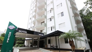 Entrada de hotel com placa, área de estar coberta ao ar livre e uma palmeira.