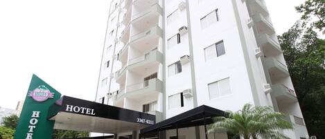 Entrada de hotel com placa, área de estar coberta ao ar livre e uma palmeira.