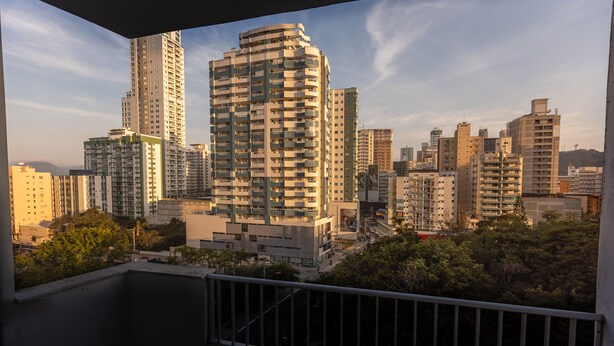 Paisagem urbana com edifícios altos, uma varanda e céu claro.
