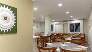 Uma área de refeições com várias mesas e cadeiras, um relógio na parede e uma peça decorativa grande à esquerda.