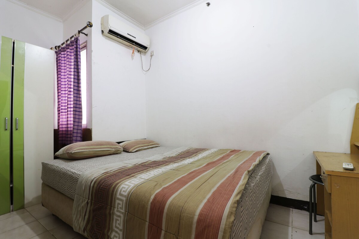 Quarto com cama, escrivaninha, guarda-roupa verde e ar condicionado.