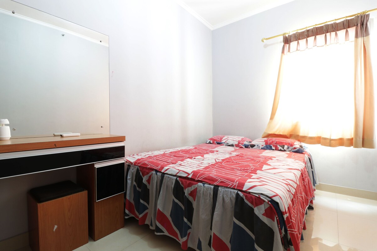 Quarto com cama, escrivaninha e janela com cortinas.