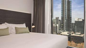 Quarto de hotel com uma cama grande, cabeceira, janela com cortinas e vista para a paisagem urbana.