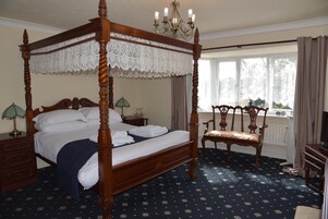 Uma cama de dossel com cortina de renda, uma cadeira de madeira, uma mesinha de cabeceira com abajur e uma janela com cortinas.