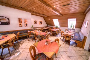 Um restaurante acolhedor com mesas e bancos de madeira, teto inclinado e obras de arte nas paredes.