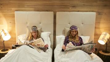 Duas camas com cabeceiras, roupa de cama branca e luminárias nas mesas de cabeceira.