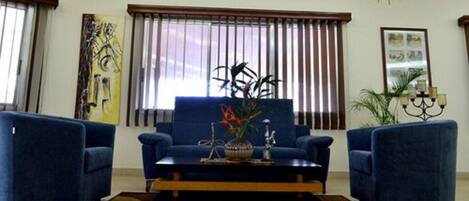 Uma sala de estar com um sofá azul, uma mesa de centro e uma janela grande com persianas.