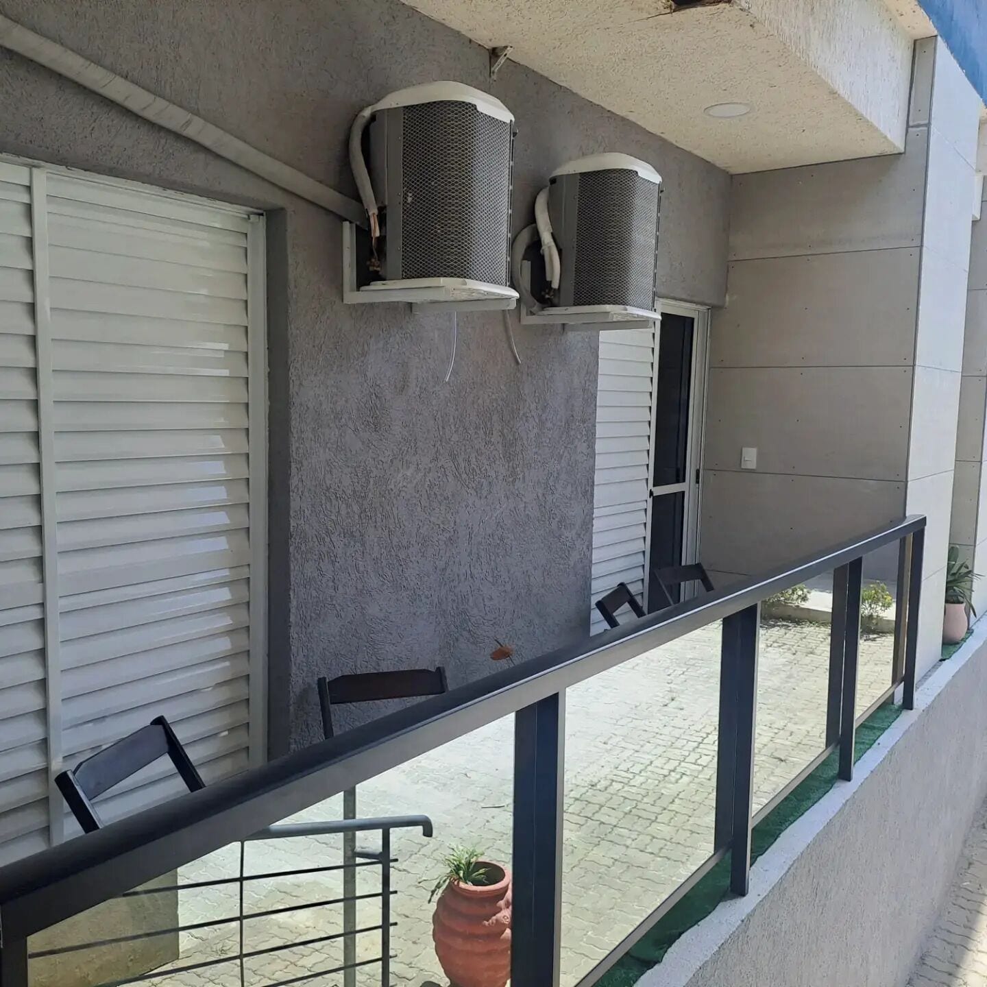 Uma varanda com duas unidades de ar condicionado, uma planta em vaso e vista para a rua.