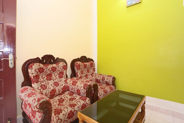 Quarto com sofá de madeira em frente a uma parede amarela, uma mesa de centro de vidro e uma porta vermelha.