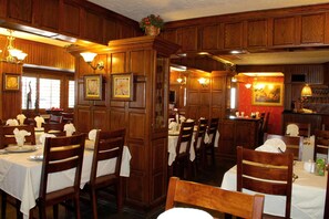 Restaurante com painéis de madeira, várias mesas com toalhas brancas e quadros com motivos florais.