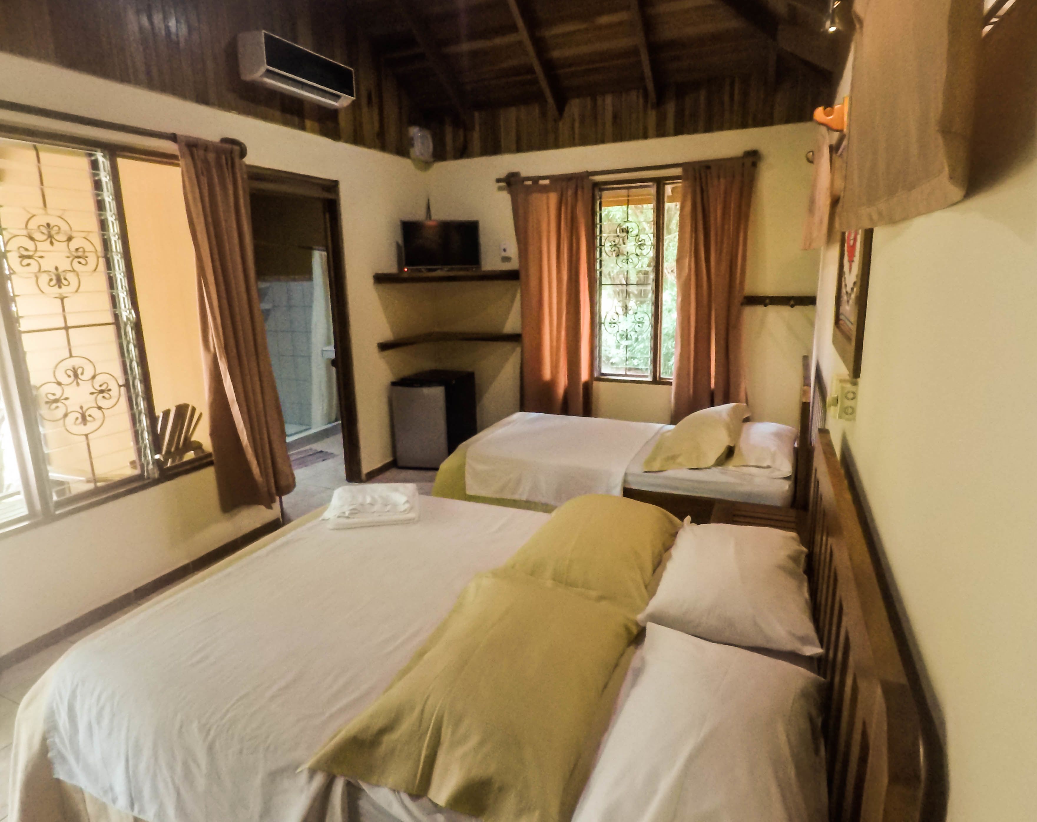 Quarto com duas camas, televisão e janela com cortinas.