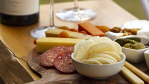 Uma mesa de madeira com diversos queijos, enchidos e uma garrafa de vinho.
