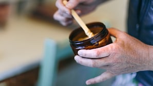 Pessoa segurando um pote com uma colher de pau dentro, provavelmente contendo algum alimento.