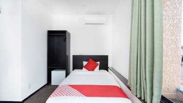 Quarto de hotel com cama, guarda-roupa, secretária e janela com cortinas.