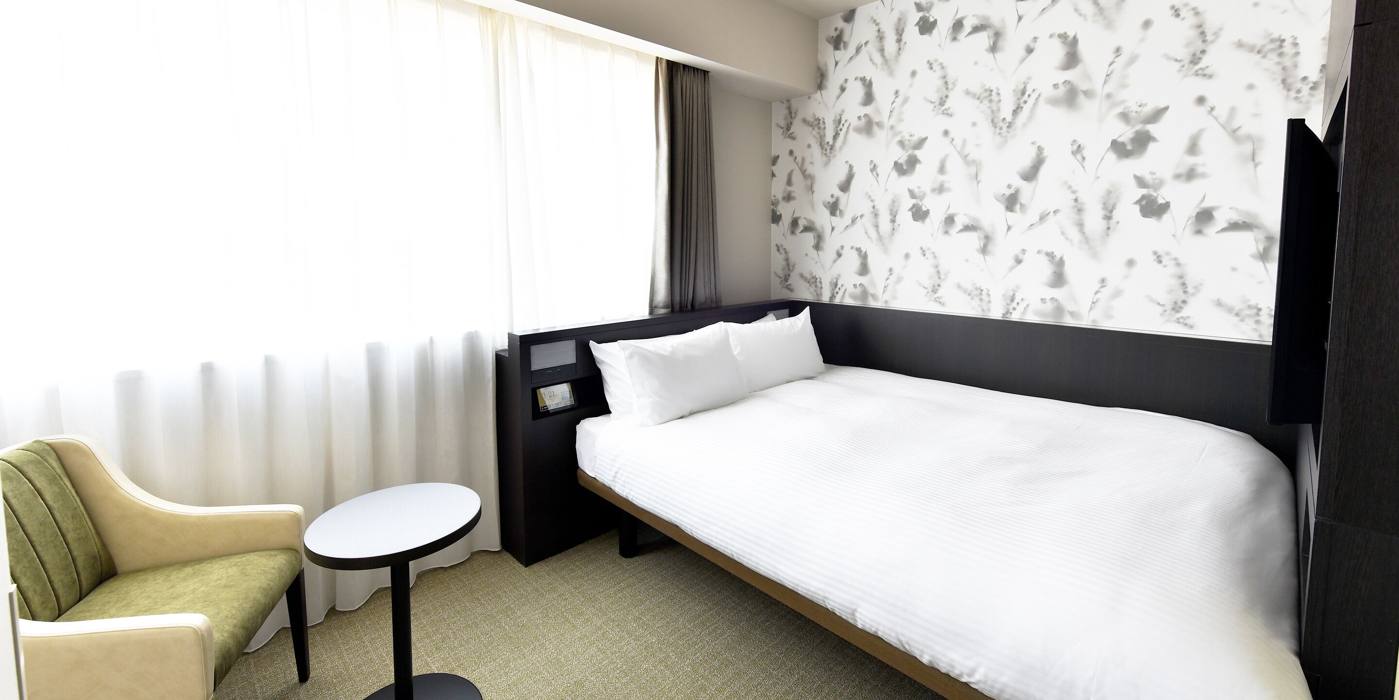 Quarto de hotel com uma cama de solteiro, uma mesinha redonda, um sofá e um criado-mudo.