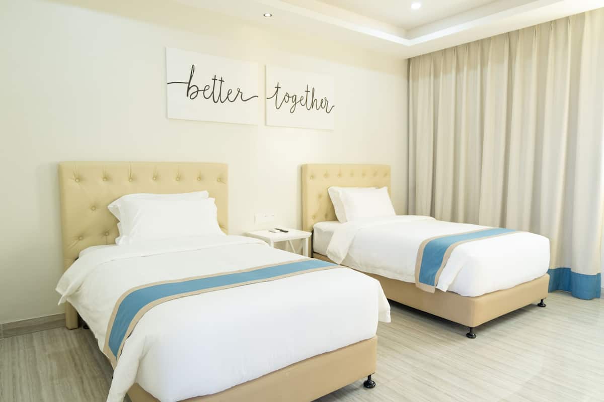 Quarto de hotel com duas camas, uma mesa de cabeceira e uma parede decorada com a frase 'better together'.