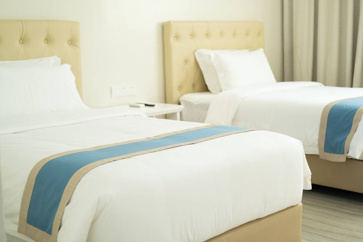 Duas camas com cabeceiras, roupa de cama branca e um detalhe azul no cobre-leito.
