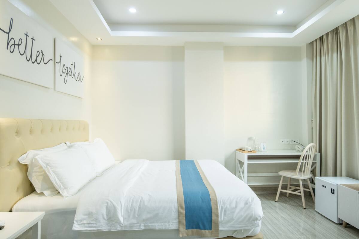 Quarto de hotel com cama, escrivaninha, cadeira e pequeno armário.