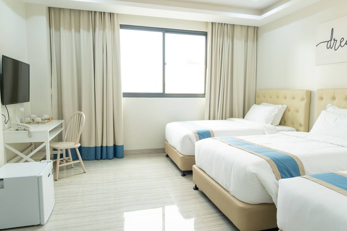 Quarto de hotel com duas camas, uma escrivaninha, uma cadeira, uma televisão e uma janela com cortinas.