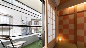 Quarto com piso de tatame, uma mesa baixa com cadeira, um painel deslizante shoji e um pequeno candeeiro.