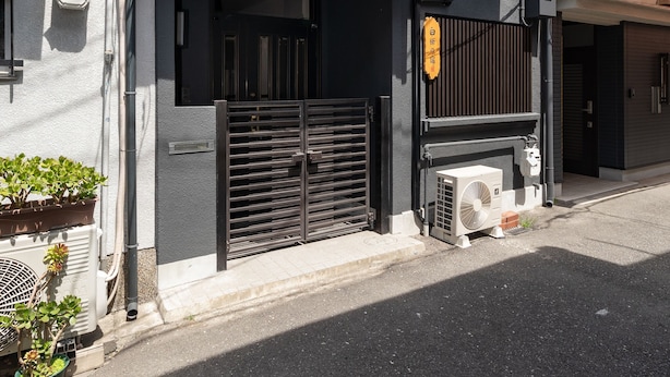 Um edifício tradicional japonês com telhado de telhas, portão preto e um pequeno aparelho de ar condicionado no andar térreo.