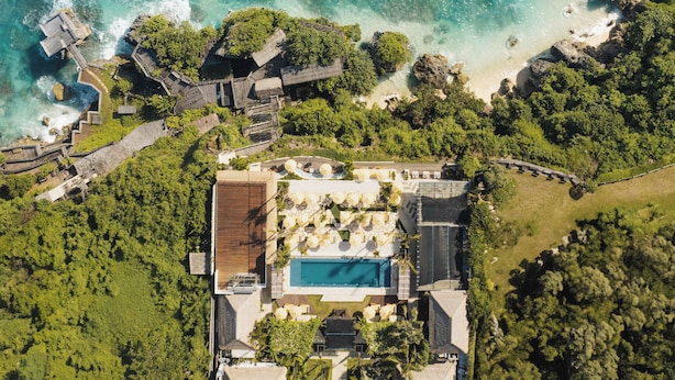 Vista aérea de um resort com piscina, vegetação exuberante e uma praia.