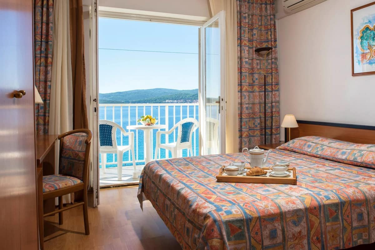 Quarto de hotel com varanda, cama com bandeja de itens de café da manhã e um quadro na parede.