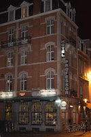 Um hotel chamado "Hotel Professor", com fachada clássica de tijolos, janelas em arco e uma placa indicando um bar de cocktails.