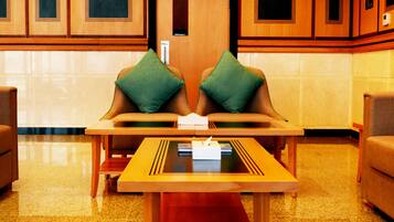 Um lobby com uma mesa de recepção, duas poltronas com almofadas verdes e uma parede de madeira com a inscrição 'PULL'.