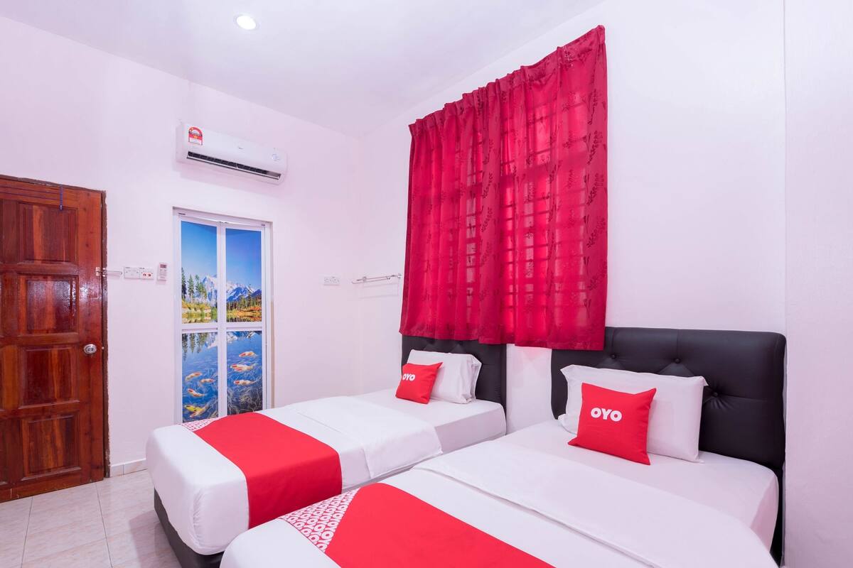 Quarto de hotel com duas camas, roupa de cama vermelha e branca, uma janela grande com vista para as montanhas e um aparelho de ar condicionado na parede.