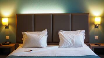 Quarto de hotel com uma cama grande, duas luminárias de cabeceira, mesa de cabeceira com um telefone e controle remoto sobre a mesa.
