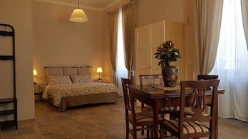 Quarto com cama, luminárias de cabeceira, mesa de jantar com cadeiras e um vaso de flores.