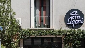 Entrada de hotel com uma placa indicando "HOTEL Ligeni", acesso coberto e plantas em vasos.