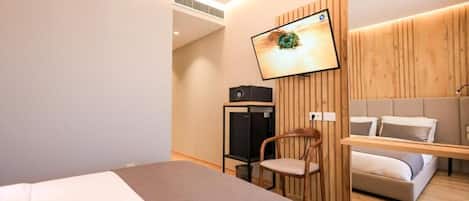 Quarto de hotel moderno com uma cama, televisão na parede, armário de madeira e um espaço de estar com sofá.