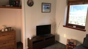 Uma sala de estar com um módulo de entretenimento de madeira escura, uma televisão de tela plana, uma mesa de centro e uma janela com vista para um parque.