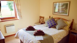 Quarto com cama, cadeira, mesa de cabeceira, janela e um quadro na parede.