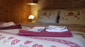 Cama bem arrumada com toalhas dobradas, colcha estampada e cabeceira de madeira.