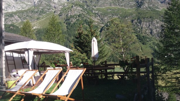 Terraço com espreguiçadeiras e um toldo branco, com vista para uma paisagem montanhosa.
