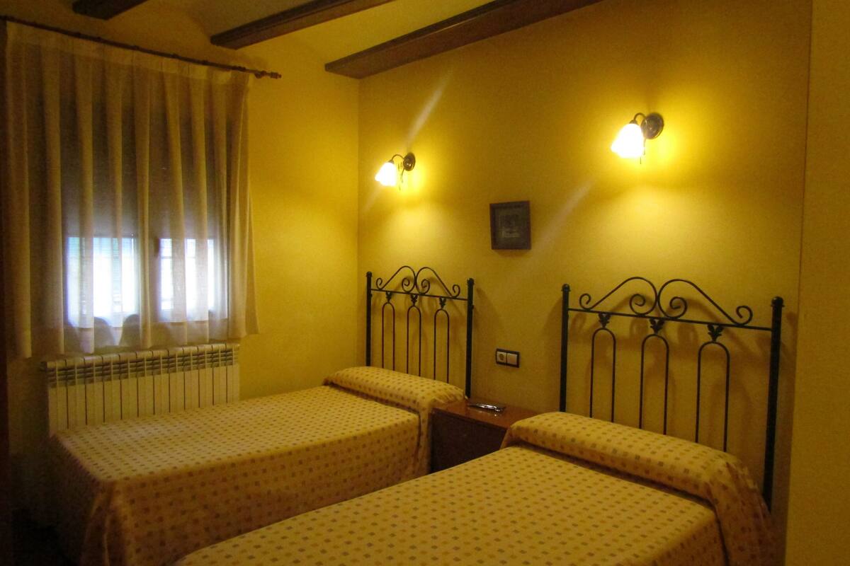 Quarto com duas camas, uma janela com cortinas e luminárias fixadas na parede.