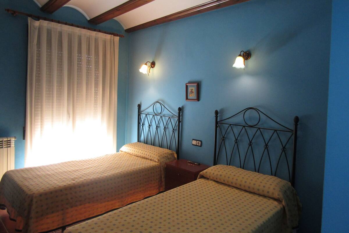 Quarto com duas camas, uma janela com cortinas e luminárias na parede.