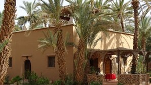 Um edifício com fachada bege, portas em arco e um terraço coberto com uma mesa vermelha.
