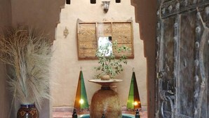 Um interior tradicional com piso de azulejos, tapete decorativo, porta de madeira e luminária fixada na parede.