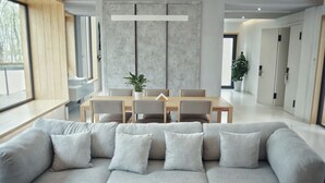 Uma sala de estar moderna com um sofá seccional cinza, uma mesa de jantar de madeira com seis cadeiras e uma grande parede cinza de destaque.