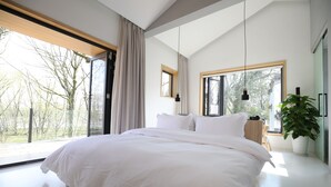Quarto moderno com uma cama grande, porta de vidro deslizante e vista para árvores.