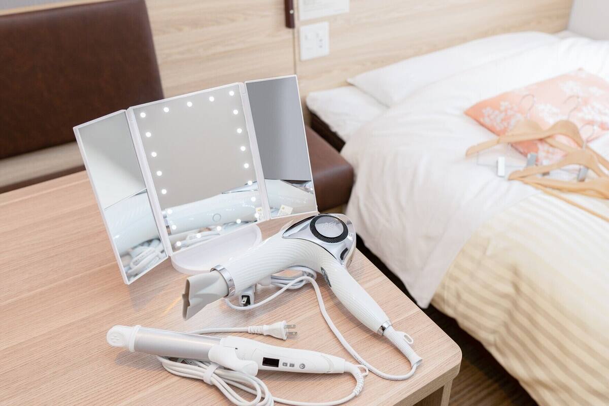 Quarto de hotel com cama, mesa de cabeceira com secador de cabelo, espelho e régua de energia.
